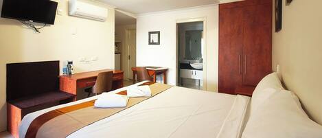 Quarto de hotel com cama, escrivaninha, cadeira, televisão e ar condicionado.