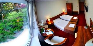 Quarto de hotel com duas camas, uma mesa de escritório e uma cadeira. Há uma janela com vista para áreas verdes lá fora.