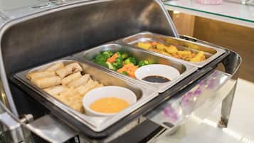 Buffet com diversos pratos, incluindo rolinhos primavera, brócolis, cenouras e molhos.