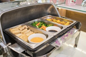 Buffet com diversos pratos, incluindo rolinhos primavera, brócolis, cenouras e molhos.