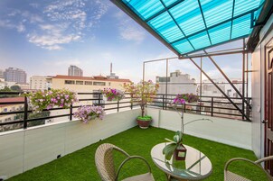 Terraço no telhado com grama sintética, móveis de vime e plantas em vasos.
