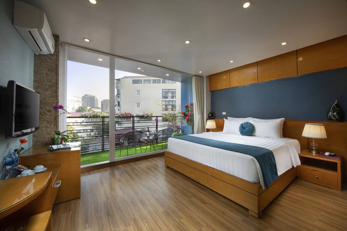 Quarto de hotel moderno com cama grande, televisão, escrivaninha e varanda com vista para a cidade.