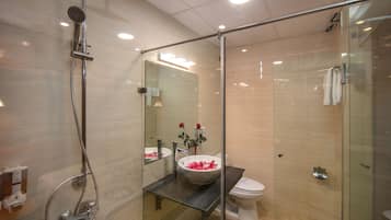 Uma casa de banho moderna com cabine de duche em vidro, lavatório branco e um vaso de rosas, e sanita.