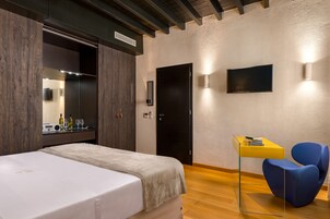 Quarto de hotel com cama, escrivaninha, cadeira, televisão e porta.
