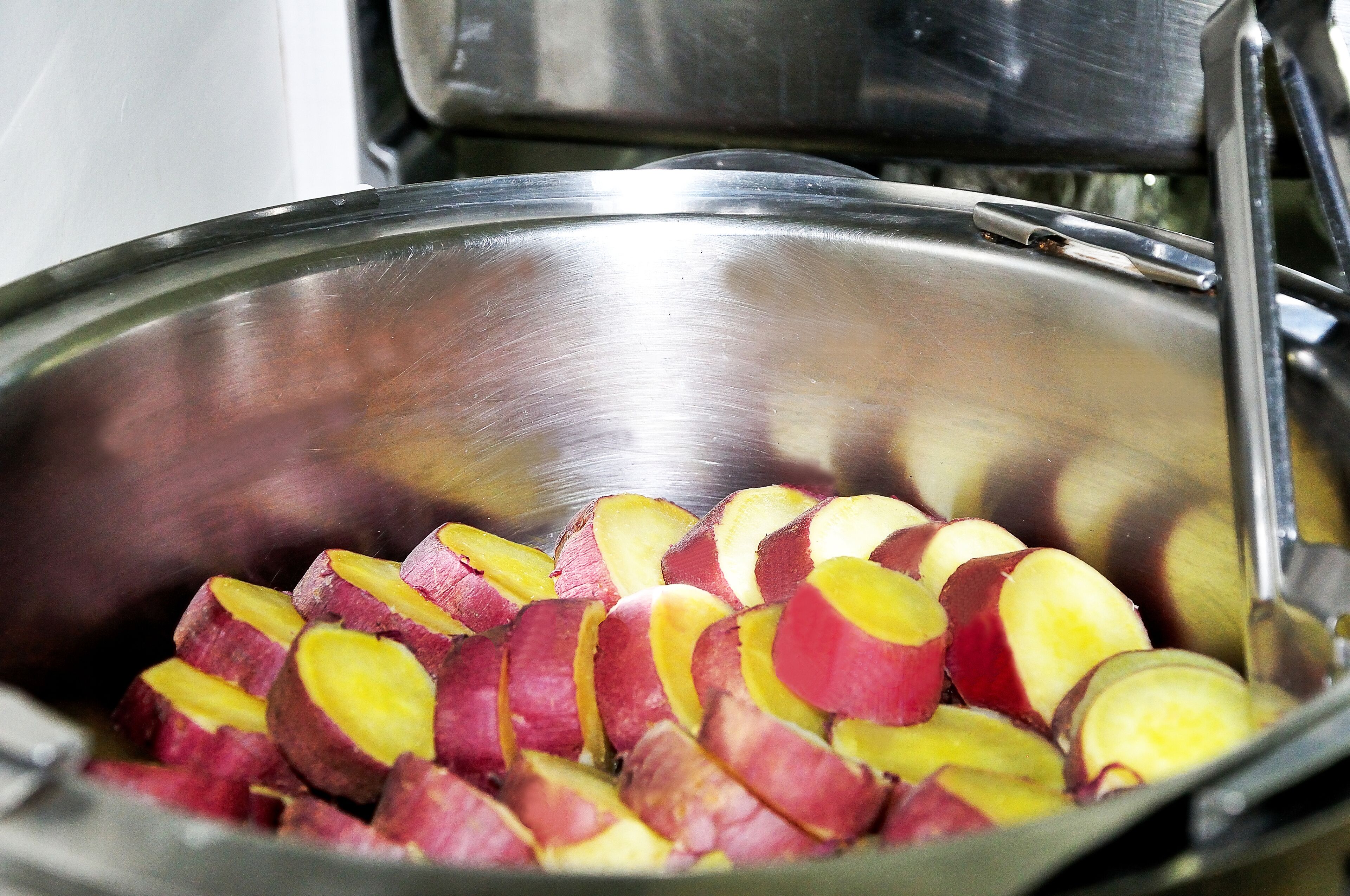 Uma tigela de aço inoxidável cheia de batata doce fatiada.