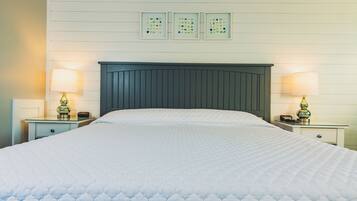 Cama bem arrumada com edredão branco acolchoado, duas mesas de cabeceira com abajures e três quadros na parede acima da cama.