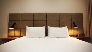 Cama bem arrumada com cabeceira, duas luminárias de apoio e uma mesinha de cabeceira com um rádio.