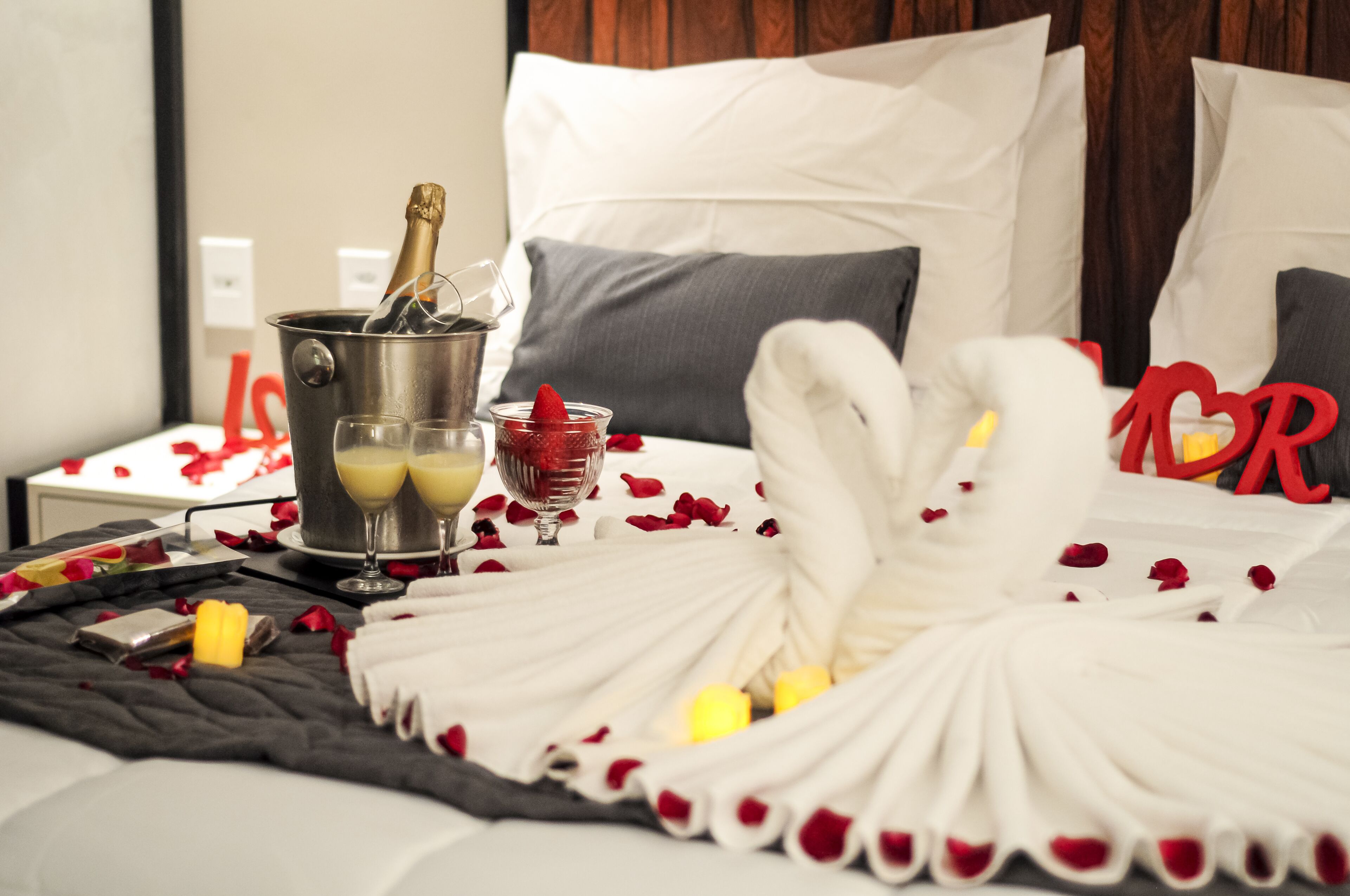Cama com toalha branca, garrafa de champanhe e taças de champanhe.