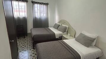 Quarto com duas camas, ventoinha no teto e piso de azulejos estampados.