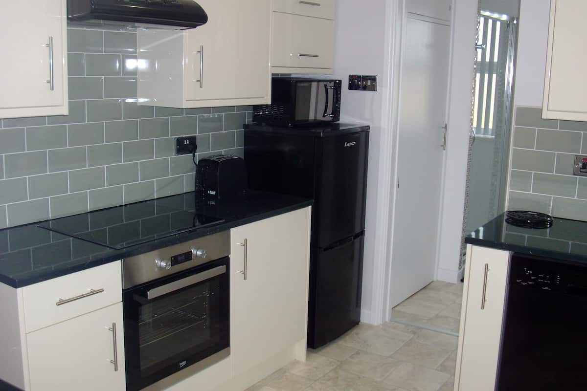 Cozinha moderna com armários brancos, eletrodomésticos pretos e painel de azulejos cinza.