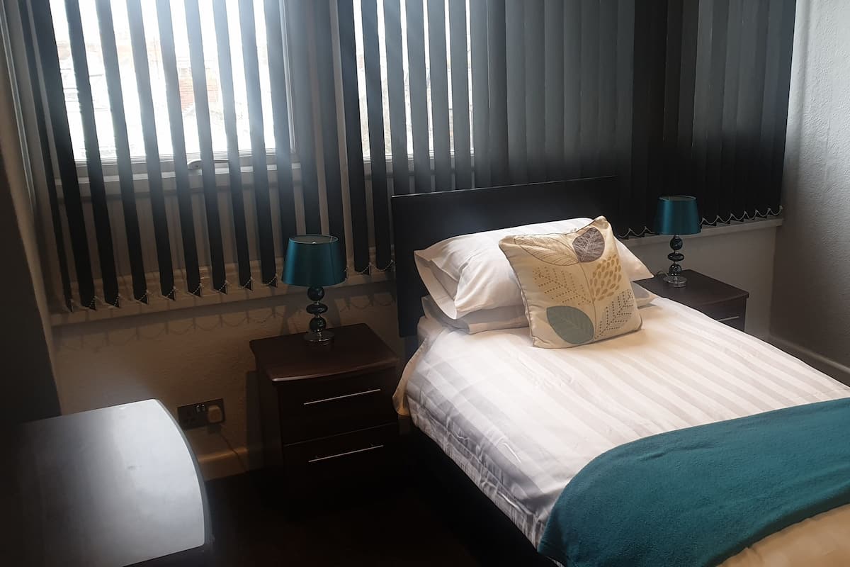 Quarto com cama, mesas de cabeceira, luminária e radiador.