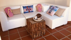 Um sofá branco modular com almofadas de tema praiano e uma mesa lateral de madeira rústica com uma tigela decorativa.