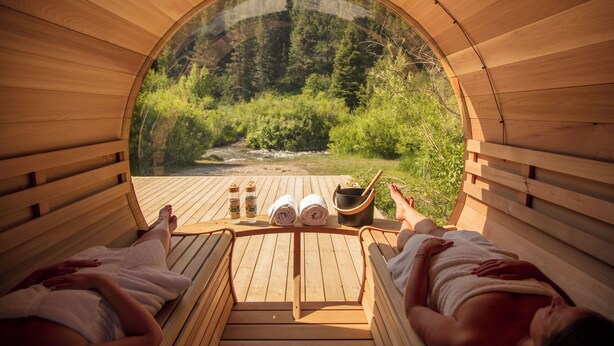 Uma cabana de madeira com uma grande janela circular, dois bancos de madeira e uma pequena mesa com garrafas e toalhas.