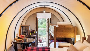 Um quarto redondo e aconchegante em estilo de tenda, com uma cama beliche, uma mesa redonda com maçãs e canecas, e uma pequena cozinha.