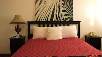 Uma cama com colcha vermelha, duas almofadas brancas, uma obra de arte de zebra na parede, um abajur em uma mesinha de cabeceira e um telefone em outra mesinha.