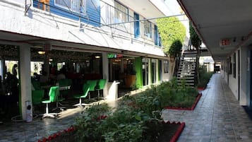 Uma área de estar coberta ao ar livre com cadeiras e mesas verdes, um pequeno jardim e uma placa de saída.