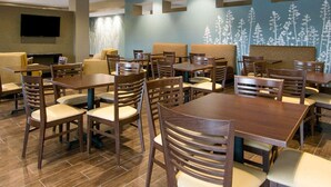 Um restaurante com várias mesas e cabines, uma televisão de tela plana na parede e um mural decorativo.