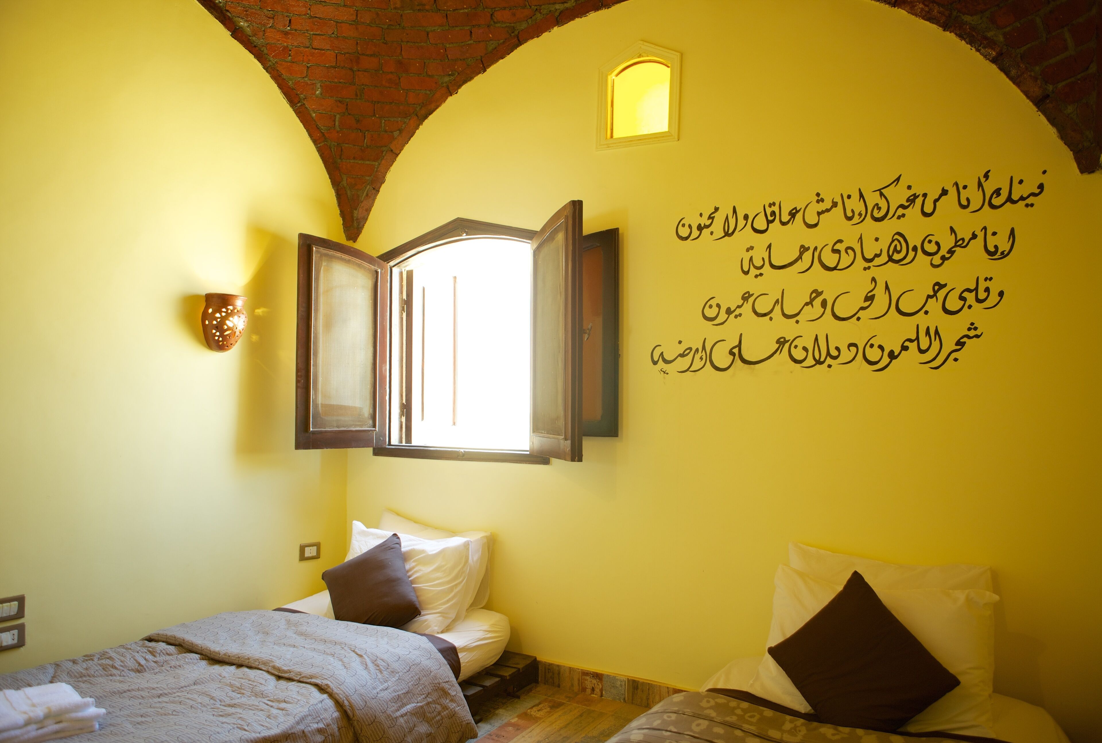 Quarto com cama, janela e parede com escrita árabe.