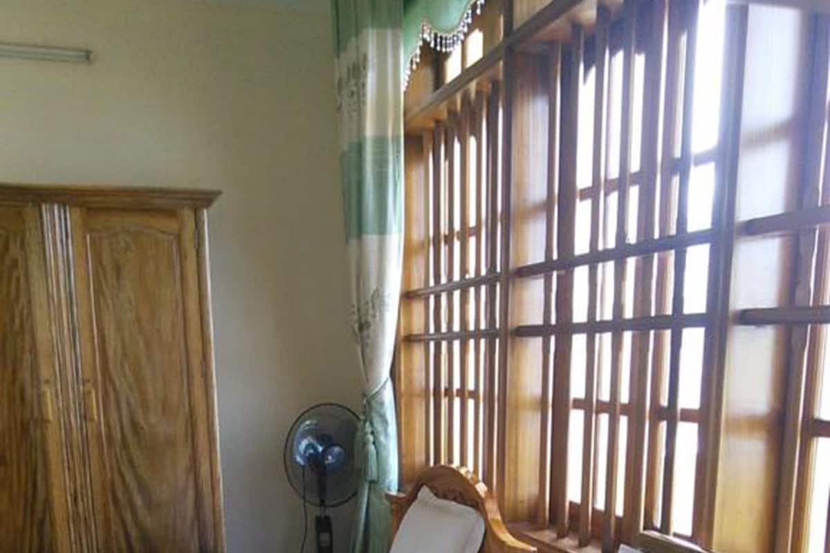 Quarto de hotel com duas camas, um guarda-roupa de madeira, um ventilador e uma janela com cortina.