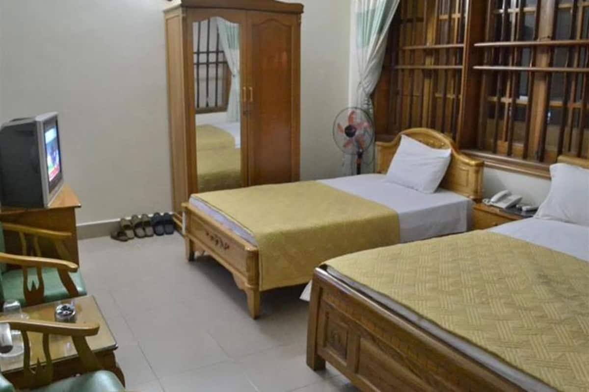 Quarto de hotel com duas camas, um guarda-roupa de madeira, uma escrivaninha com cadeira, televisão e uma janela com grades.