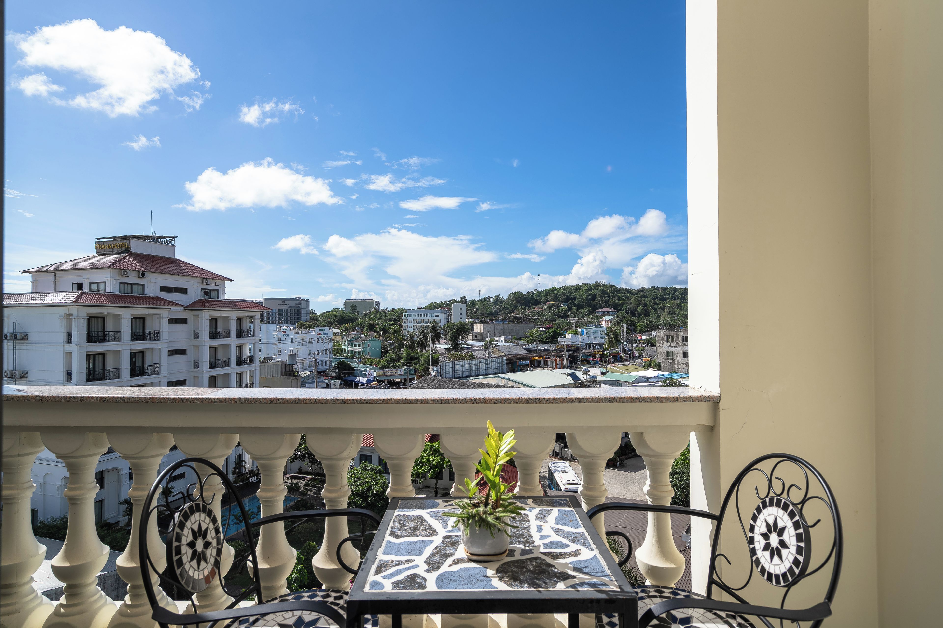 Uma varanda com mesa e cadeiras, com vista para um horizonte urbano com edifícios e uma colina.