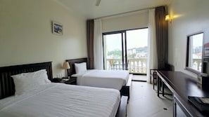 Quarto de hotel com duas camas, uma escrivaninha, uma cadeira, janela com vista para edifícios e um quadro na parede.