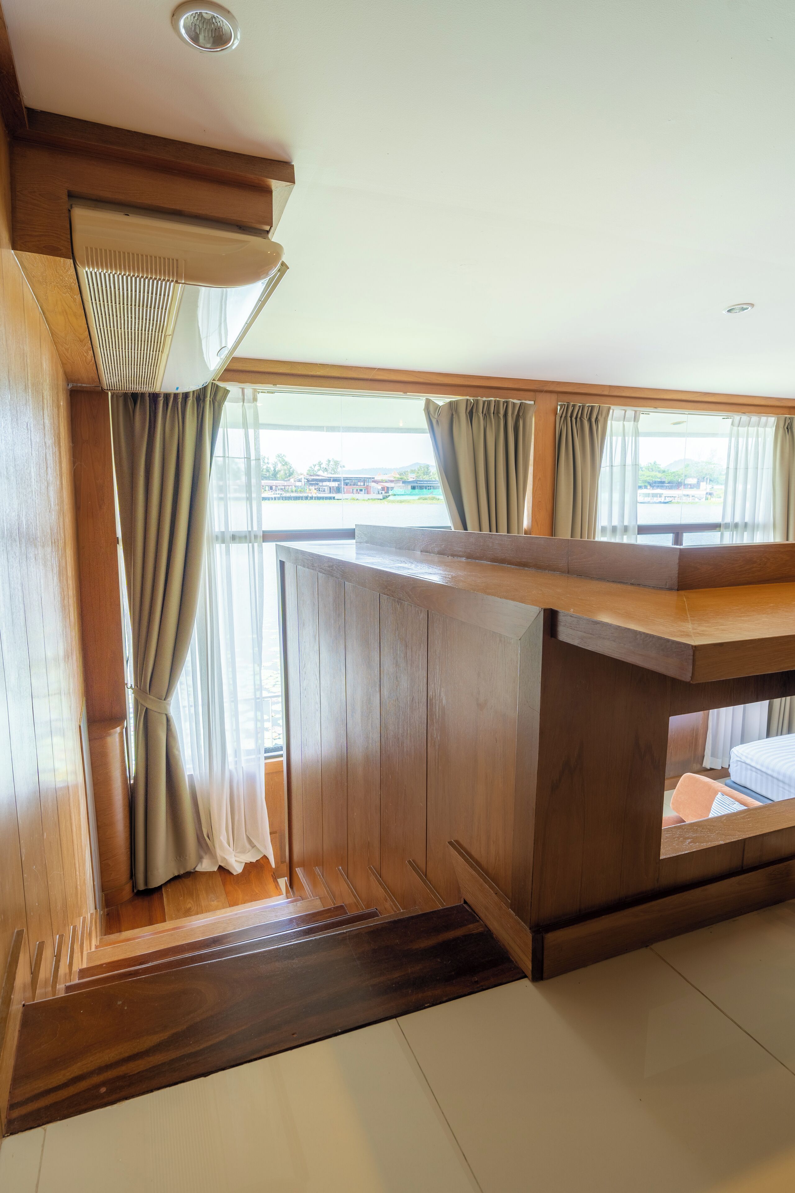 Quarto com um banco de madeira, uma mesa pequena e vista para o exterior através de janelas amplas.