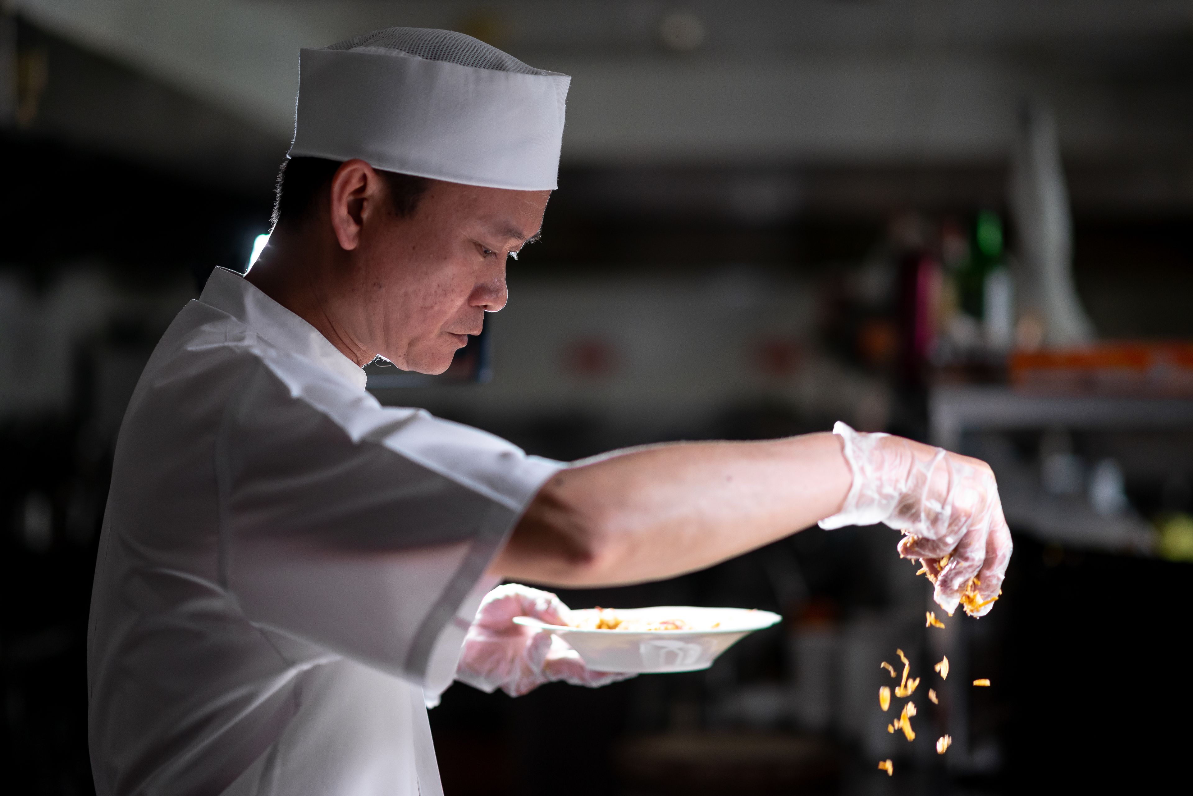 Um cozinheiro de uniforme e chapéu branco, segurando um prato com restos de comida.