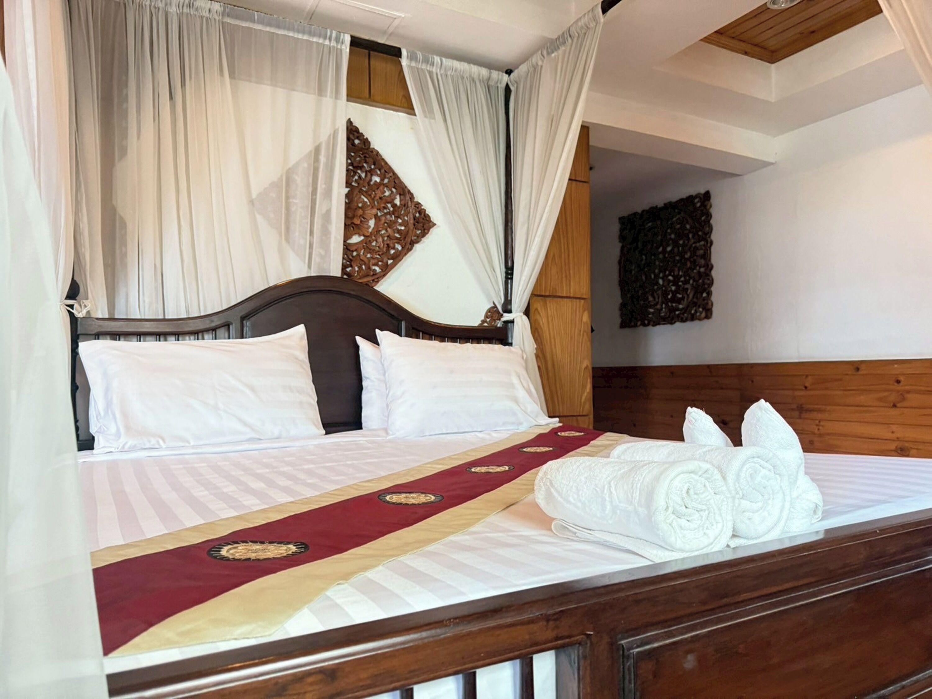 Uma cama com dossel, cabeceira de madeira e colcha vermelha e dourada.