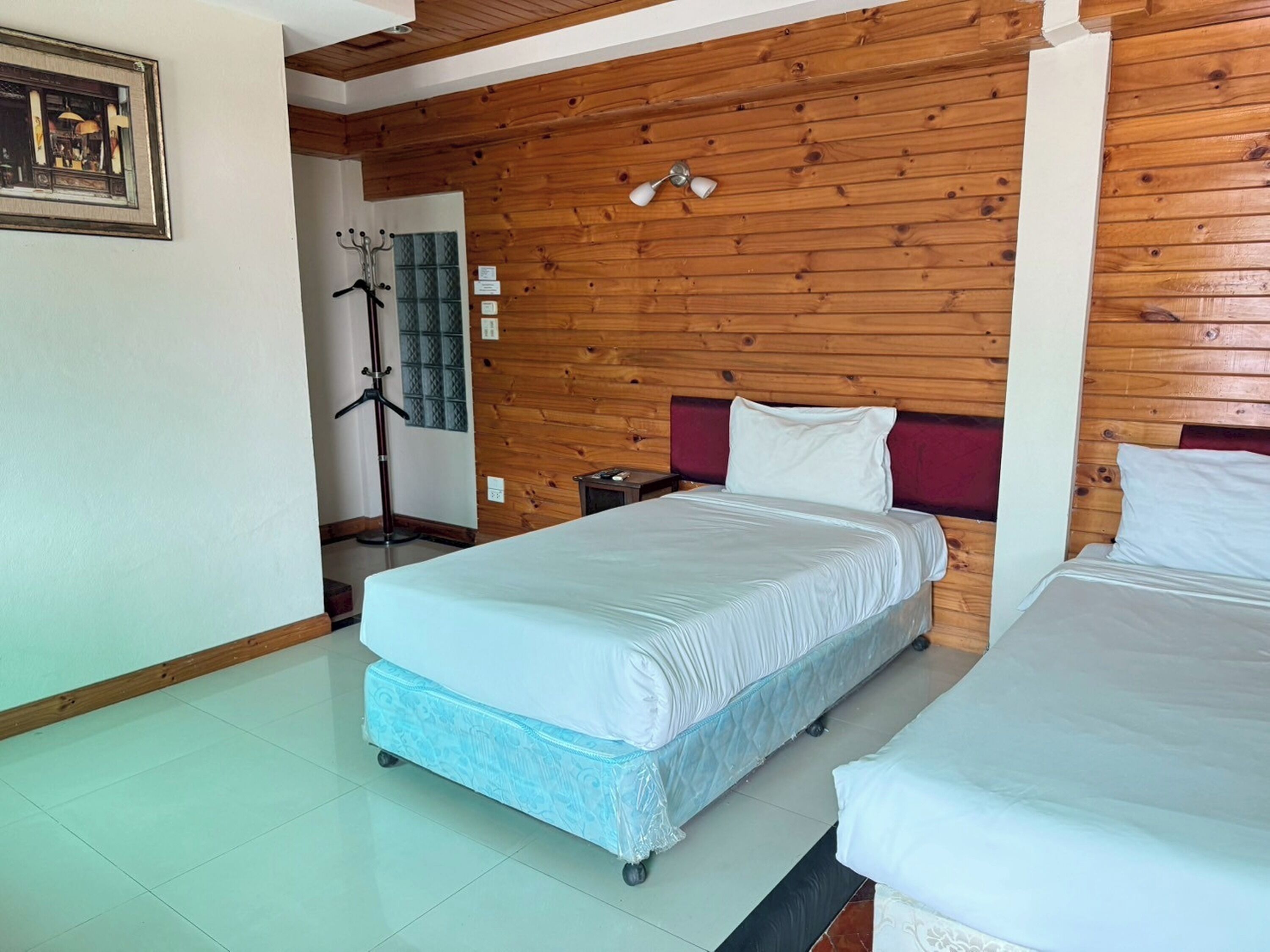 Quarto com duas camas, paredes de painel de madeira, um ventilador de teto e um abajur.