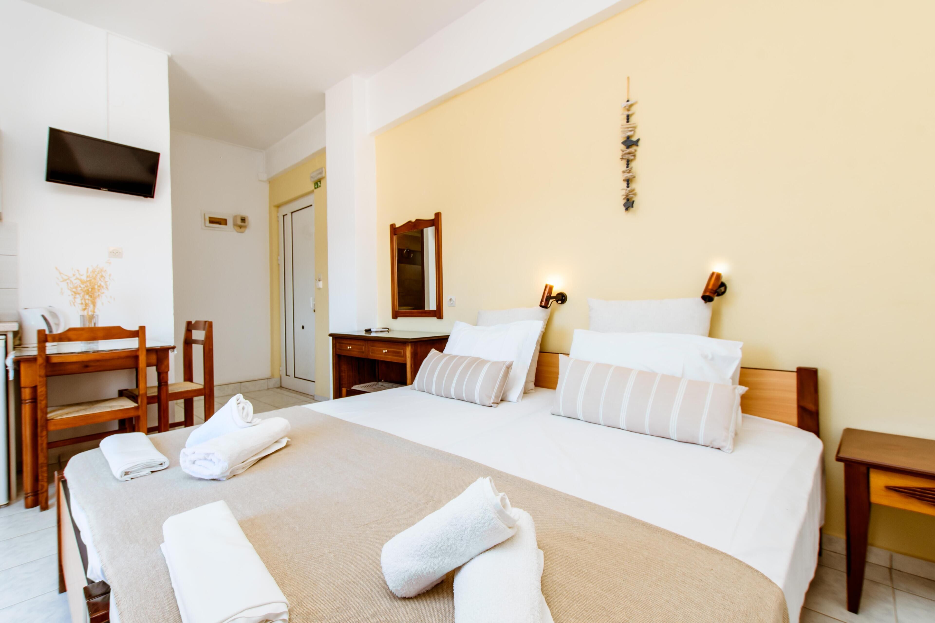 Quarto de hotel com uma cama grande, duas mesas de cabeceira, uma escrivaninha, uma cadeira e uma televisão na parede.