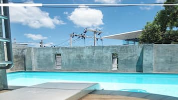 Área de piscina com deck de madeira, paredes de concreto e céu azul límpido.