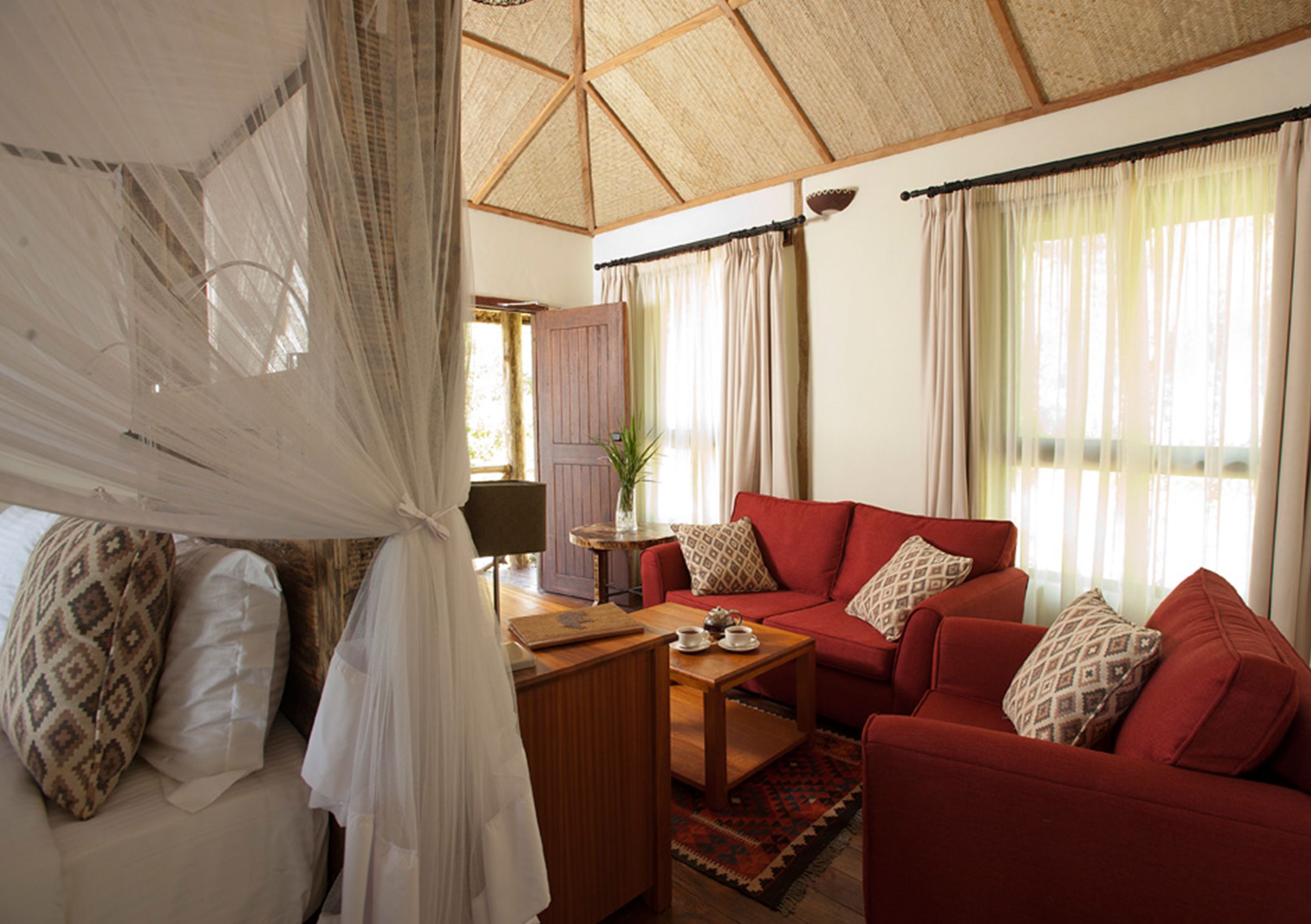 Quarto com uma cama, um sofá vermelho, uma mesa de centro de madeira e vista para o exterior através de grandes janelas.