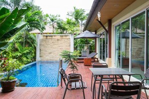 Área da piscina com deck de madeira, espreguiçadeiras e uma pequena mesa.