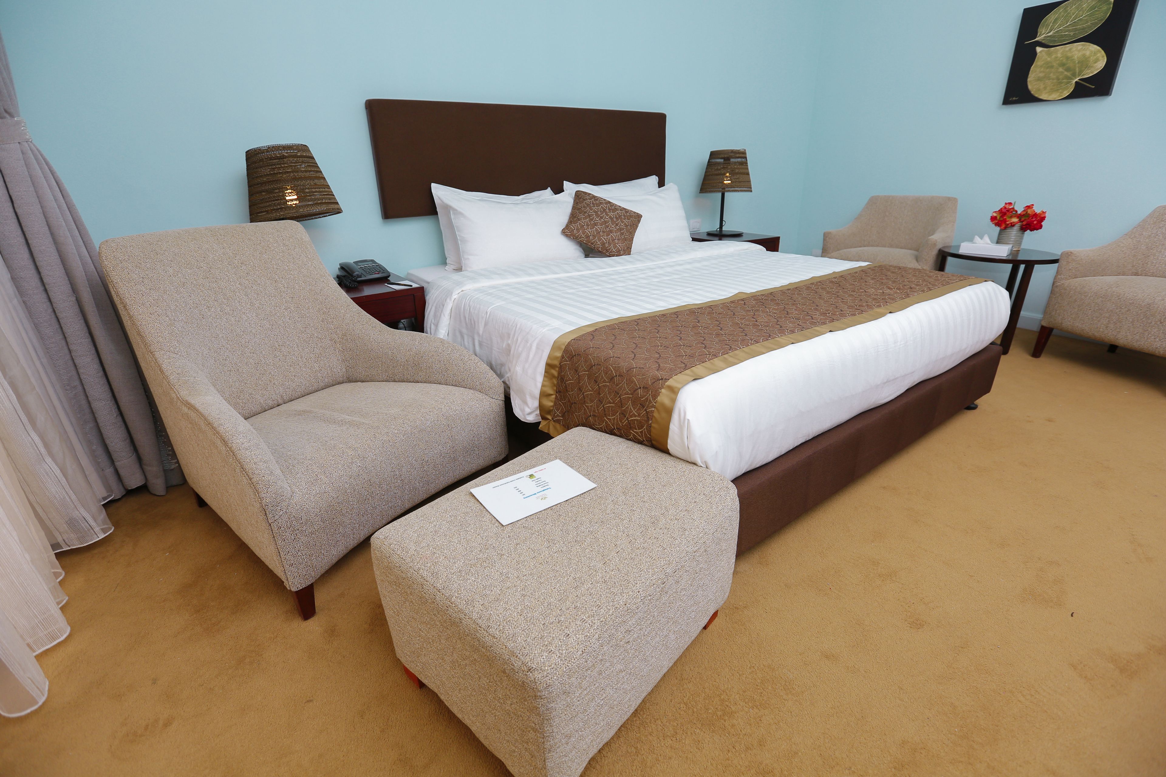 Quarto de hotel com uma cama grande, duas poltronas, uma mesinha e um abajur.