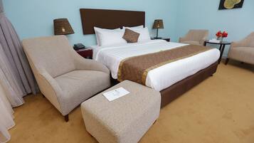 Quarto de hotel com uma cama grande, duas poltronas, uma mesinha e um abajur.