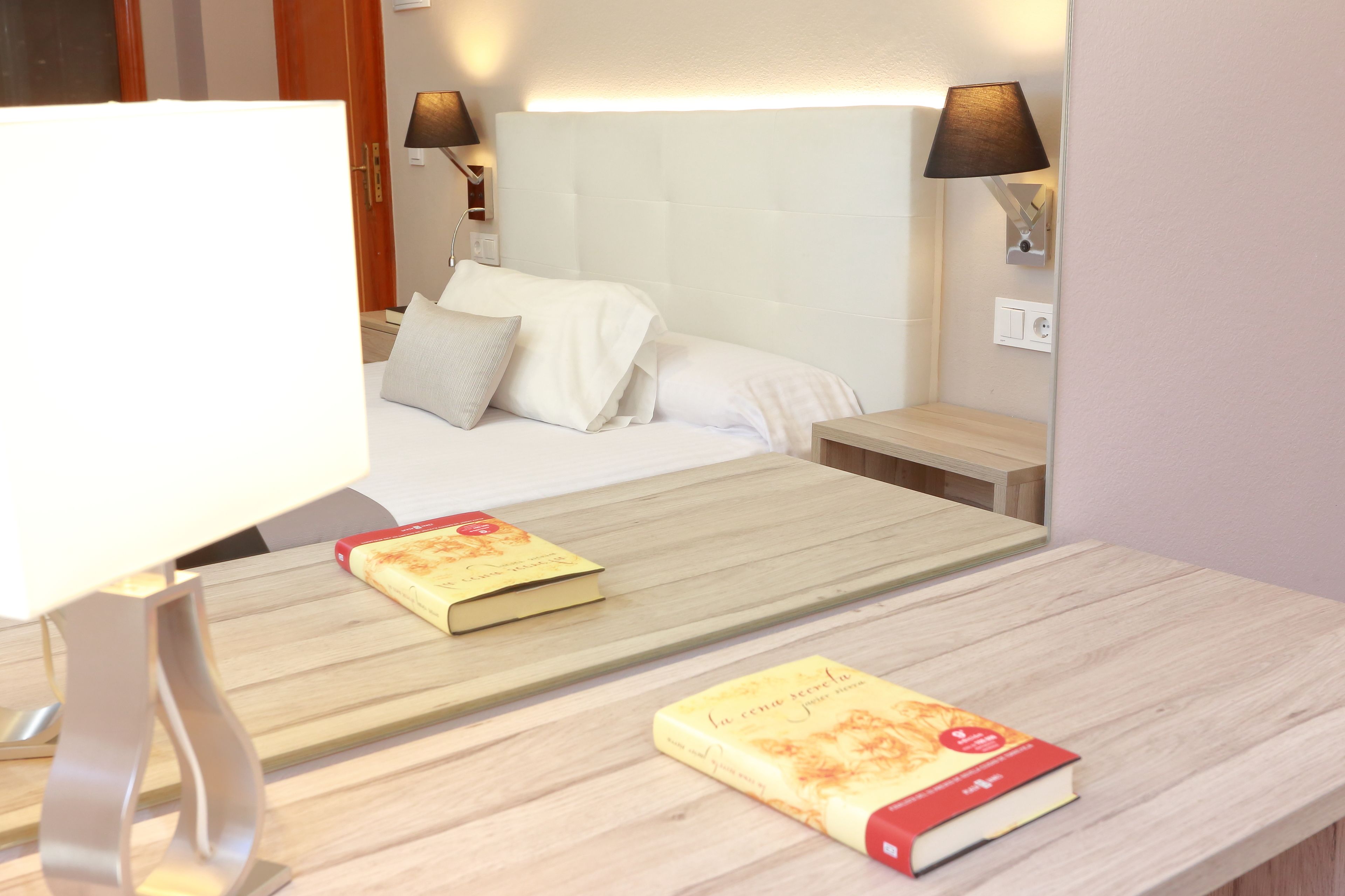 Quarto de hotel com uma cama, mesas de cabeceira e dois livros na mesinha de apoio.