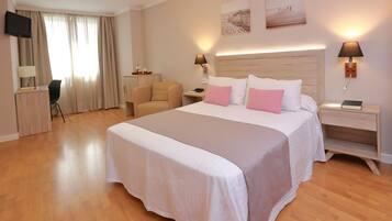 Quarto de hotel com uma cama grande, uma escrivaninha, uma cadeira, uma televisão e uma janela com cortinas.