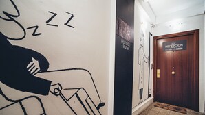 Uma área de recepção com uma porta de madeira, uma parede com a placa 'Pension Irune' e uma parede com um desenho de uma pessoa dormindo.