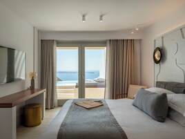 Quarto de hotel moderno com cama grande, televisão de tela plana, mesa de cabeceira e vista para o mar através de uma porta de vidro deslizante.