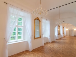 Um quarto espaçoso com grandes janelas, lustres elaborados e piso de parquet.