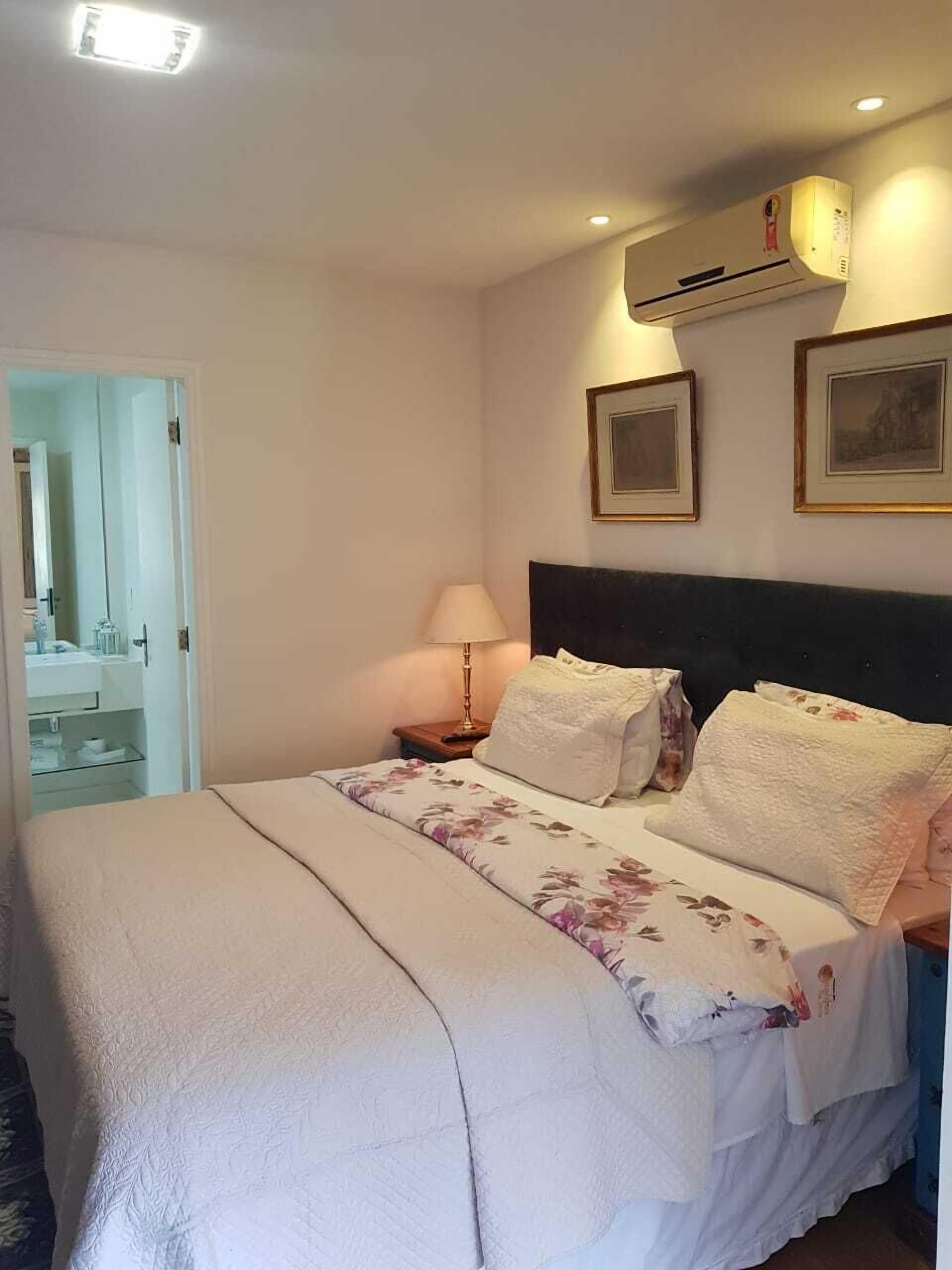 Uma cama bem arrumada com roupa de cama florida, uma luminária de cabeceira e um ar condicionado fixado na parede.