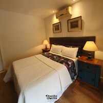 Uma cama bem arrumada com um edredom estampado com flores, duas mesas de cabeceira com abajures e um ar condicionado fixado na parede.