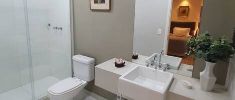 Uma casa de banho moderna com cabine de duche em vidro, sanita, lavatório e espelho.