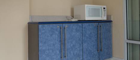 Um armário azul com um micro-ondas em cima, um aviso com os horários de funcionamento do micro-ondas e uma porta com painel de vidro.