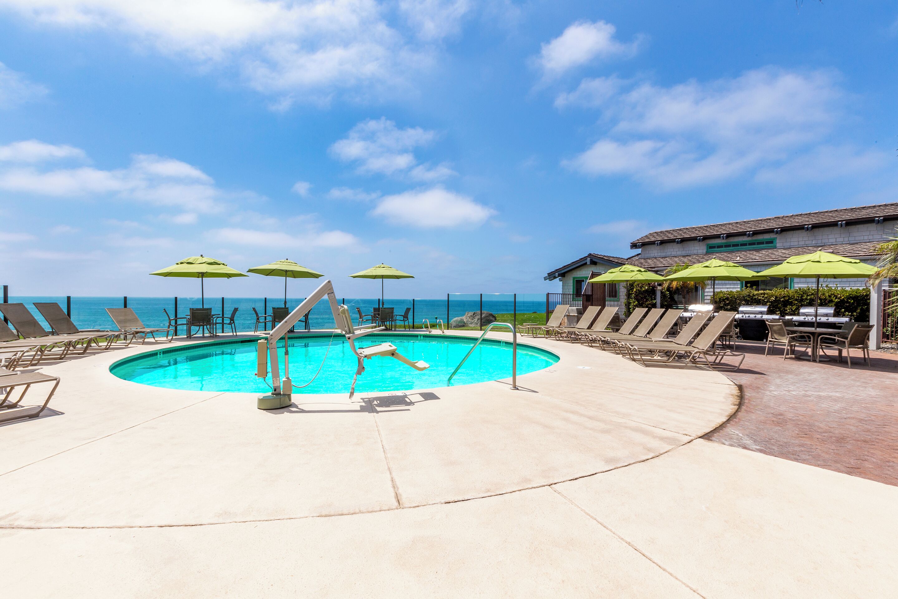 Uma área de piscina com espreguiçadeiras e guarda-sóis, uma piscina e vista para o oceano.