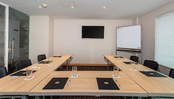 Sala de conferências com uma mesa comprida, cadeiras, quadro branco e tela de projeção.