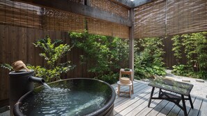 Uma banheira de hidromassagem numa varanda de madeira, com cerca de bambu e vegetação ao fundo.