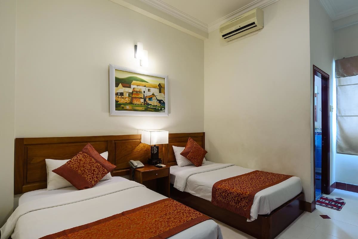 Quarto de hotel com duas camas, um quadro na parede, abajur, telefone e ar condicionado.