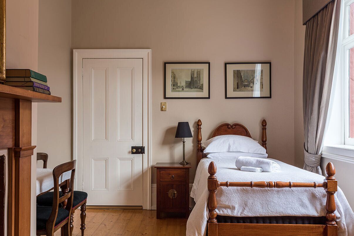 Quarto com cama de madeira, mesa de cabeceira com luminária, cadeira, estante e duas quadros pendurados na parede.